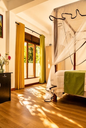 Quarto com cama de dossel, piso de madeira e janela com cortinas.