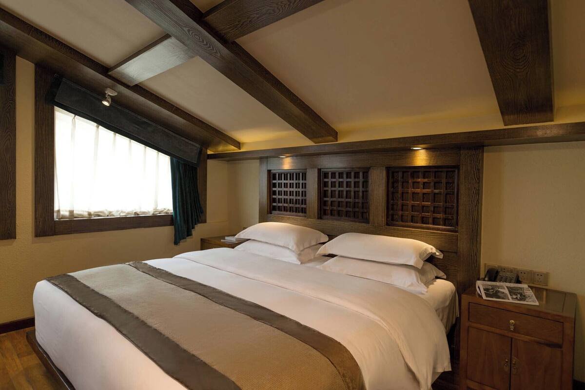 Quarto com cama grande, cabeceira de madeira, mesa de cabeceira e janela com cortinas.