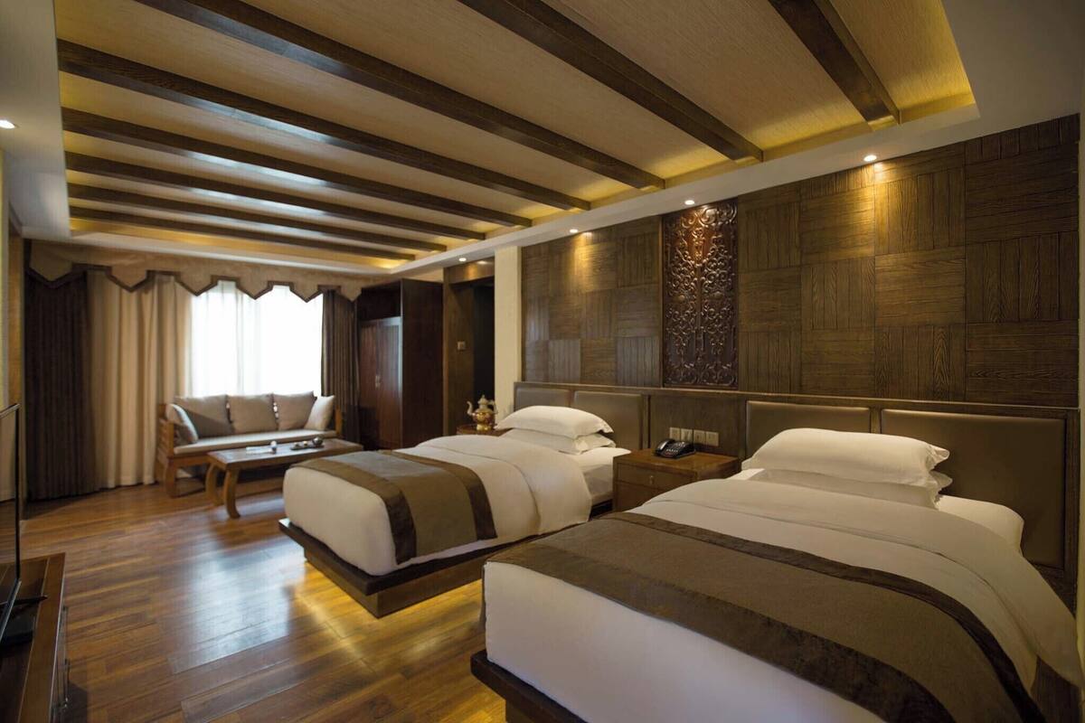 Quarto de hotel com duas camas, um sofá, piso de madeira e um painel decorativo na parede.