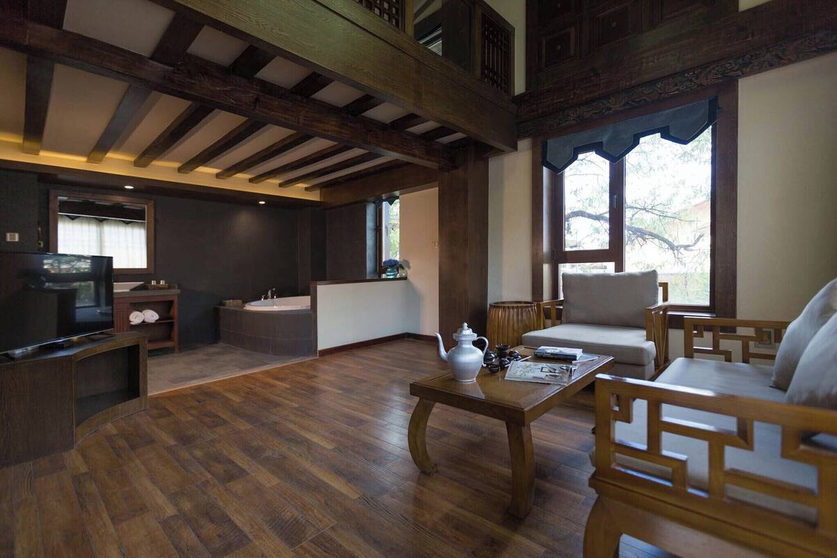 Um quarto amplo com piso de madeira, um sofá, uma mesa com um bule e uma televisão.