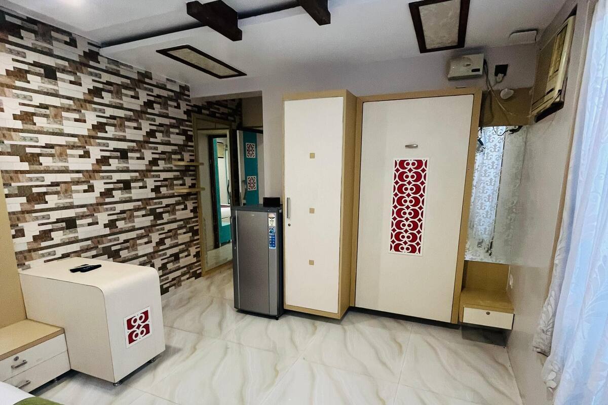 Quarto de hotel com piso de azulejos, uma cama, um pequeno espaço para sentar, um guarda-roupa e um frigorífico.