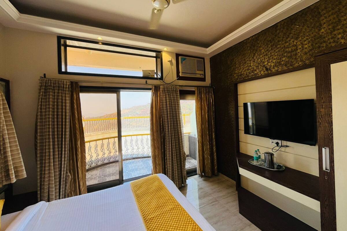 Quarto de hotel com cama, televisão, varanda com cortinas e ar condicionado.