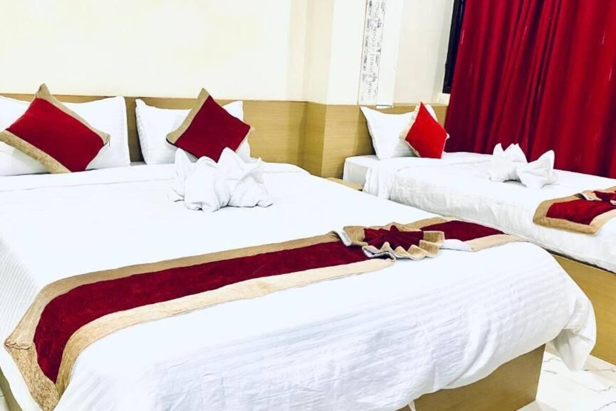Quarto de hotel com duas camas, cada uma com roupa de cama branca e detalhes vermelhos, e uma cortina vermelha.
