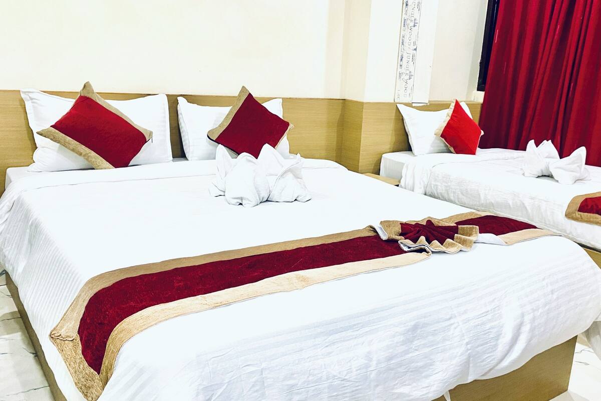 Quarto de hotel com duas camas, cada uma com roupa de cama branca e detalhes vermelhos, cortina vermelha e cabeceira de madeira.