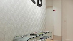 Uma área de recepção com uma vitrine de vidro, uma placa na parede com uma letra e uma porta identificada com o número '03'.