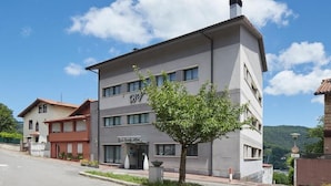 Um hotel com vários andares, fachada moderna, entrada visível e uma árvore em primeiro plano.