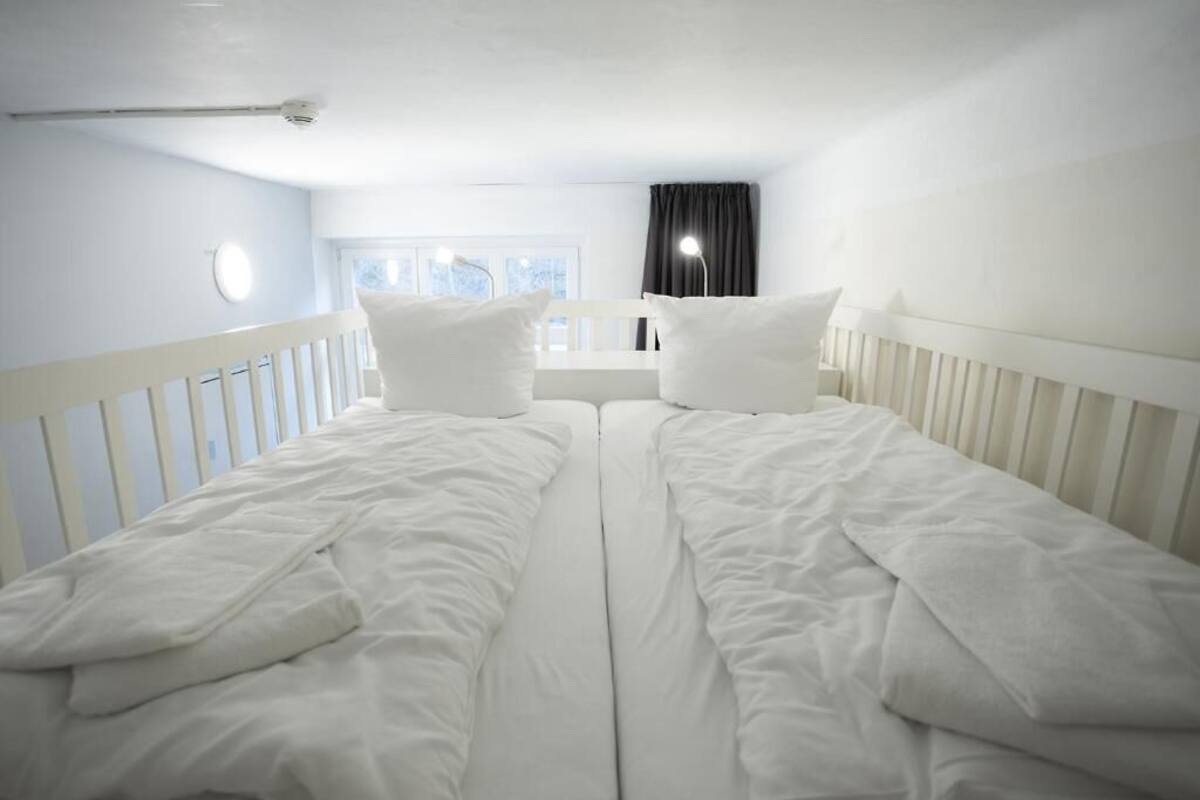 Quarto duplo com duas camas, uma janela com cortinas e um corrimão branco.