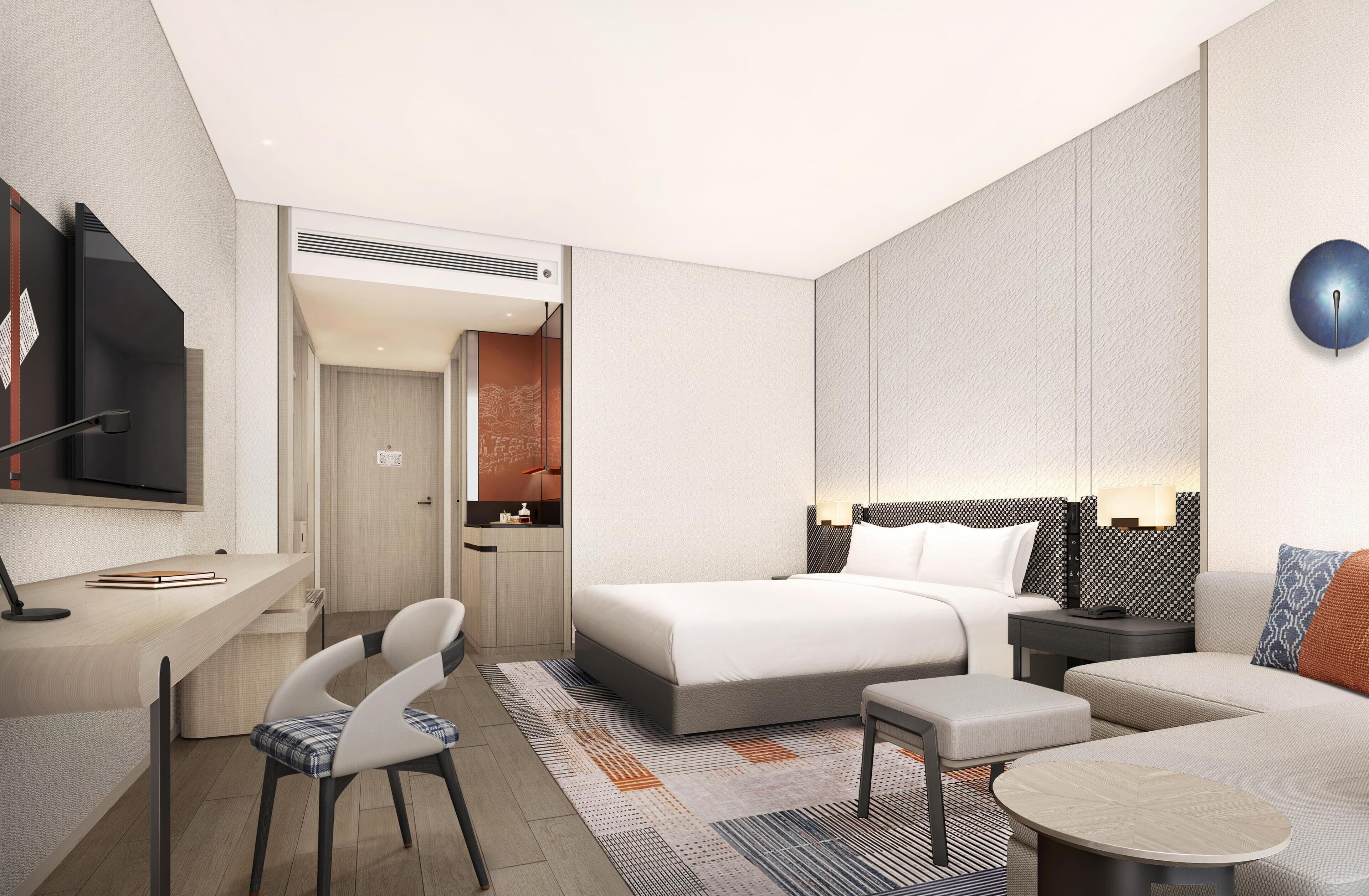 Quarto de hotel moderno com cama, escrivaninha, cadeira, sofá e TV.