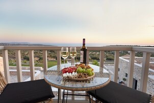 Varanda com mesa posta para dois, com tábua de queijos, uvas, nozes e duas taças de vinho branco.