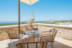 Terraço com móveis de vime e uma mesa, com vista para a paisagem costeira.