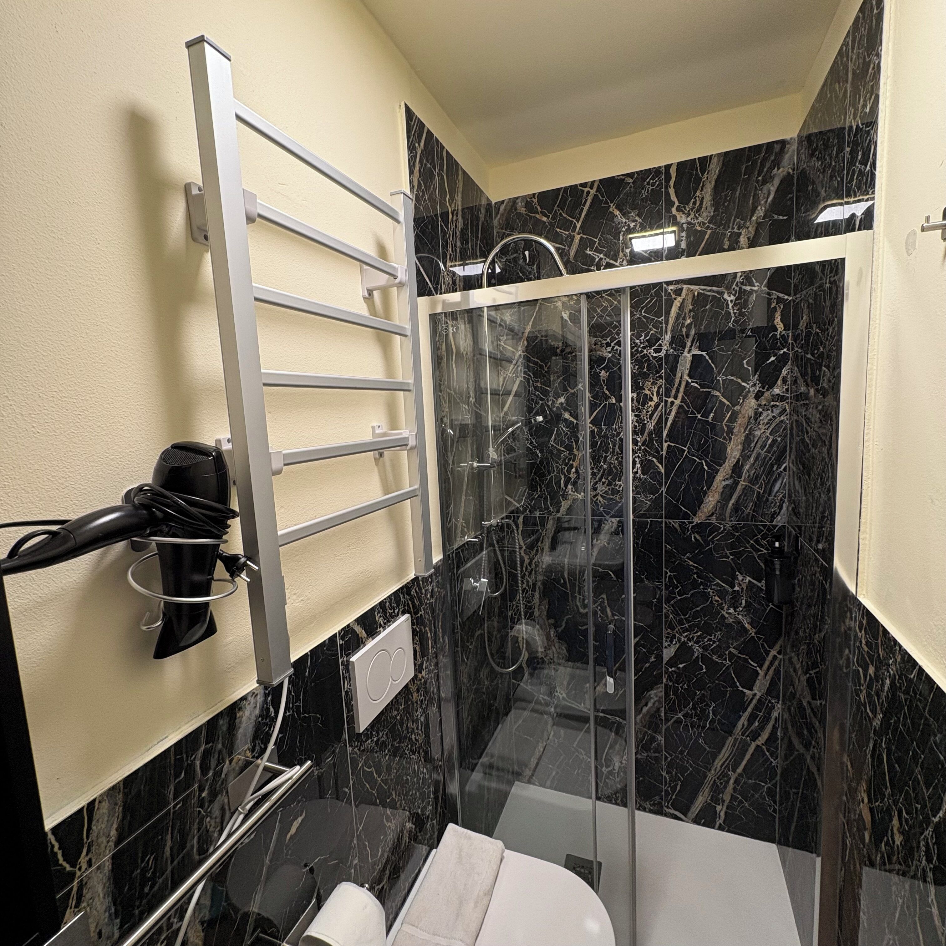 Uma casa de banho moderna com cabine de duche em vidro, um porta-toalhas e um secador de cabelo.