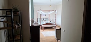 Quarto com cama de dossel, mesa de cabeceira com abajur e uma cadeira.