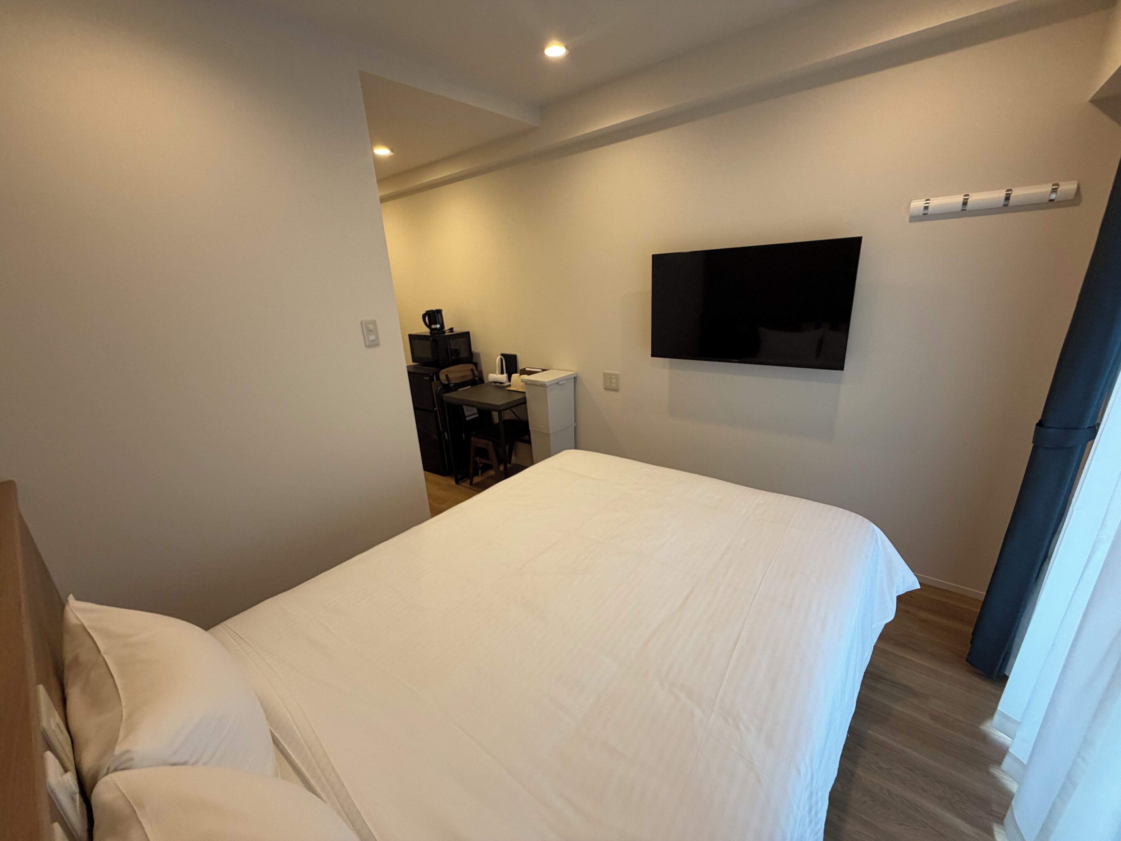 Quarto de hotel com uma cama, uma escrivaninha com cadeira, uma televisão na parede e uma janela.