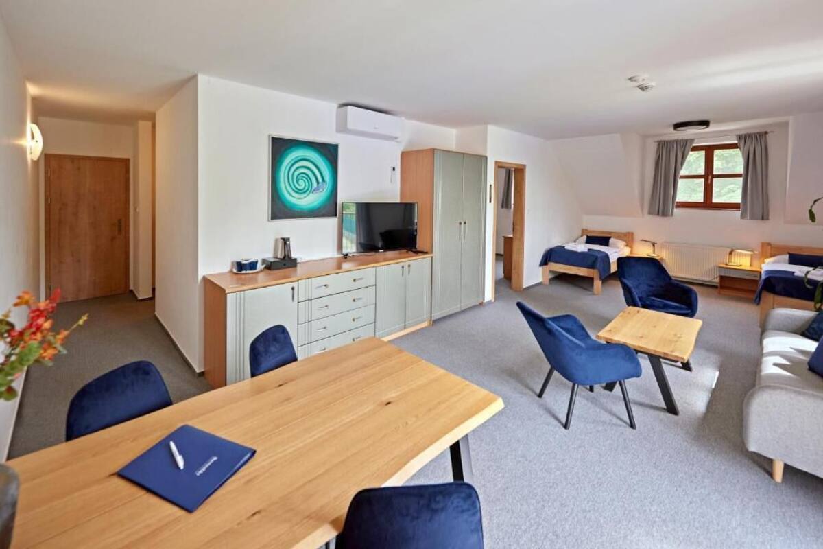 Quarto de hotel moderno com área de jantar, sofás e televisão.
