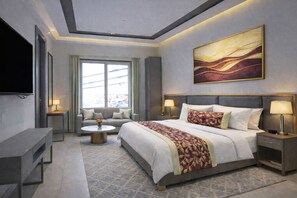 Quarto de hotel moderno com uma cama grande, um sofá, uma TV e um quadro na parede.