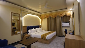 Quarto de hotel com cama, escrivaninha, cadeira, espelho, ventoinha de teto e ar condicionado.