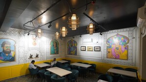 Um restaurante com mesas e cadeiras, murais nas paredes e luminárias pendentes.