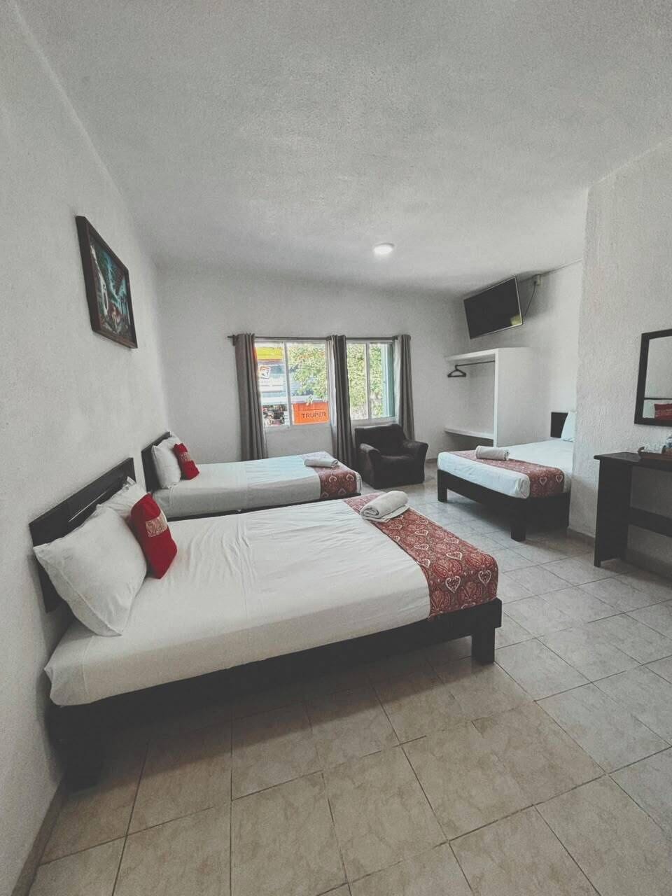 Quarto de hotel com duas camas, televisão, uma cadeira e janela com cortinas.