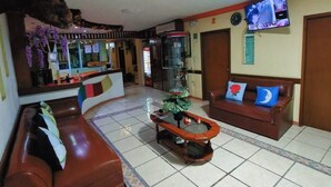 A hotel lobby with a reception desk, a brown sofa, a coffee table, and a television mounted on the wall.