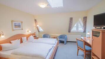 Quarto de hotel com uma cama de casal, uma escrivaninha, uma cadeira, uma televisão e uma janela com cortinas.