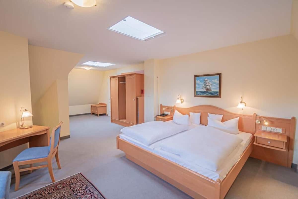 Quarto de hotel com cama, escrivaninha, cadeira, mesas de cabeceira e um quadro na parede.
