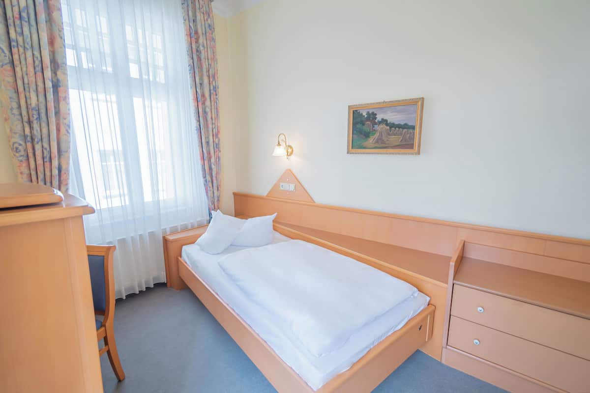 Um quarto com uma cama, mesa de cabeceira, cômoda, abajur e um quadro na parede.