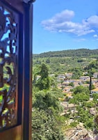 Vista de uma aldeia no topo de uma colina, com edifícios tradicionais, vegetação densa e céu limpo.