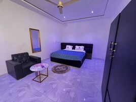 Quarto com cama, sofá preto, mesinha, espelho e guarda-roupa.