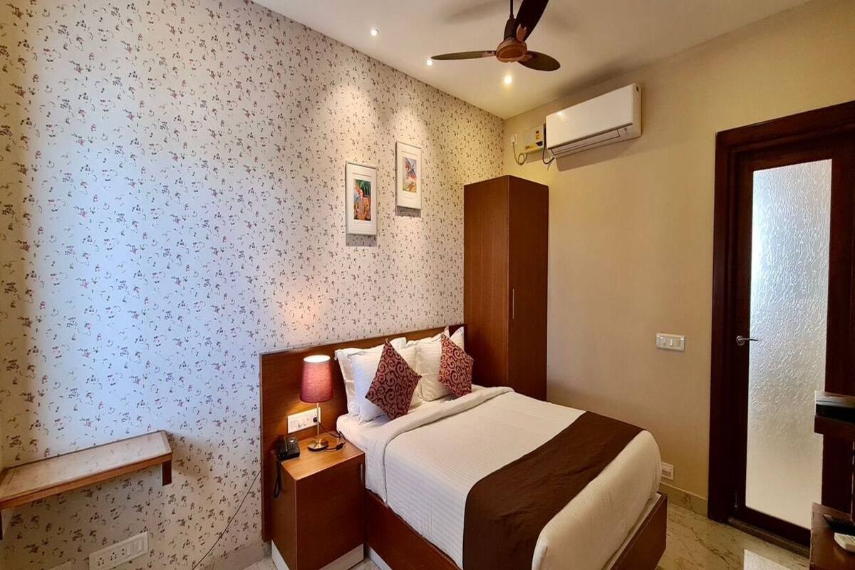 Quarto de hotel com cama, mesa de cabeceira, ar condicionado fixado na parede e ventoinha no teto, além de uma porta.