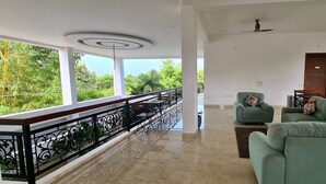 Quarto espaçoso com varanda, poltronas verdes, ventilador de teto e vista para o verde.
