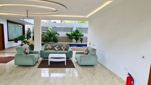 Uma sala de estar moderna com piso de mármore, um conjunto de sofás, uma mesa de centro e vista para uma piscina.
