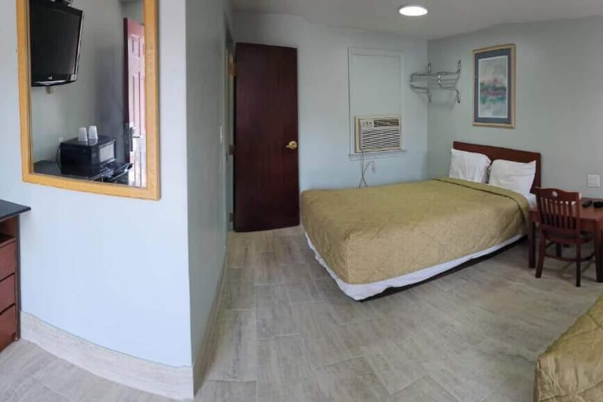 Quarto de hotel com duas camas, uma escrivaninha, uma cadeira, televisão e guarda-roupa.