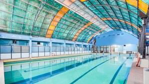 Piscina interna com teto de vidro e paredes azuis.