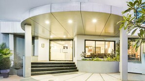 Entrada de um edifício moderno com telhado curvo, portas de vidro e escadaria que leva ao interior.