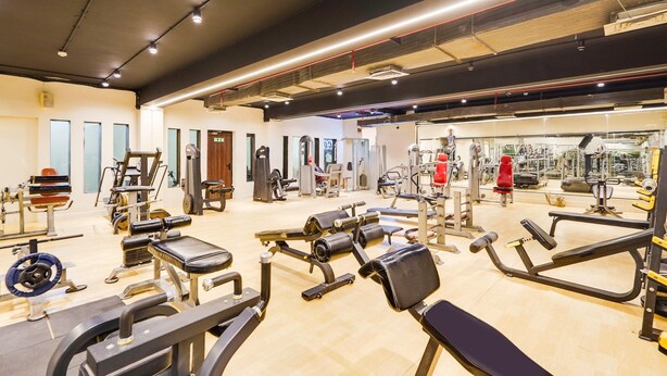 Uma academia com diversos equipamentos de exercício, incluindo bancos, máquinas de musculação e equipamentos de cardio.