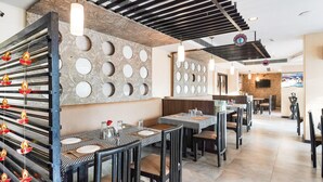 Um restaurante com decoração moderna, apresentando um balcão comprido com cadeiras pretas, parede com padrão e recortes circulares e luminárias pendentes.