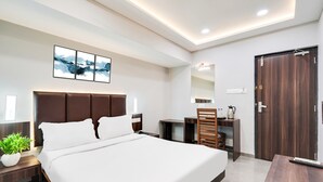 Quarto de hotel moderno com uma cama grande, uma escrivaninha, uma cadeira, uma planta em vaso e um guarda-roupa.