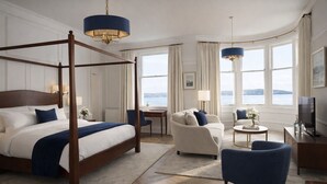 Uma cama de dossel com vista para o mar, um espaço de estar com uma poltrona e mesa, e uma televisão sobre um móvel.