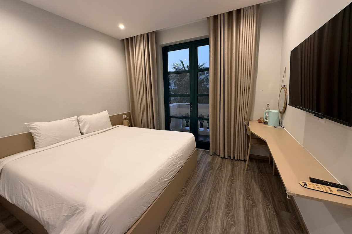 Quarto de hotel com cama, escrivaninha, televisão e janela com cortinas.