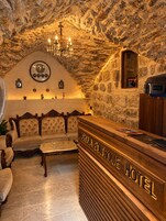 Um hall de hotel com parede de pedra, um candelabro, um sofá, um balcão de recepção e um relógio na parede.
