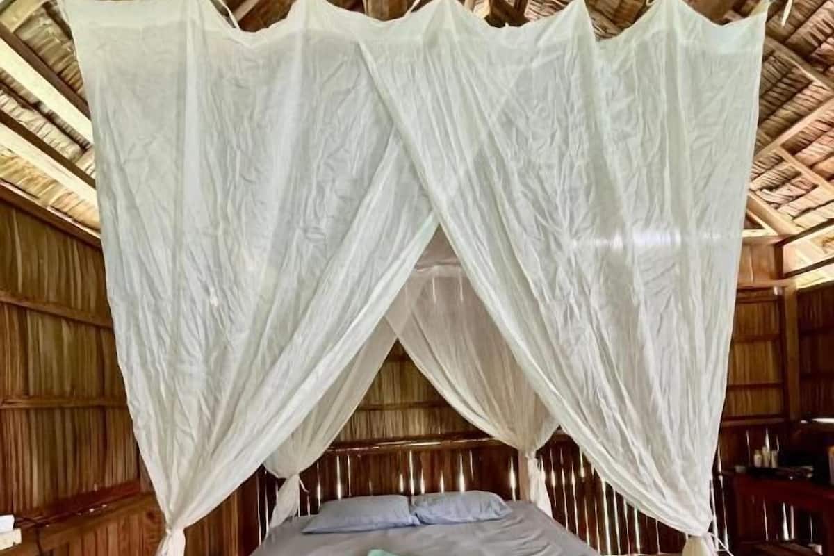 Uma cama com dossel, paredes de madeira e um telhado de palha.
