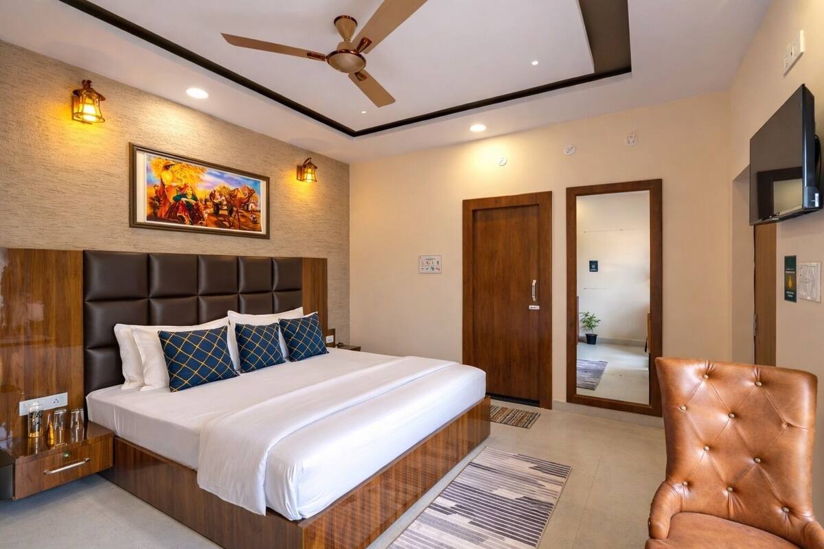 Quarto de hotel com uma cama grande, um ventilador de teto, uma cabeceira de madeira, uma TV fixada na parede e uma porta com espelho.