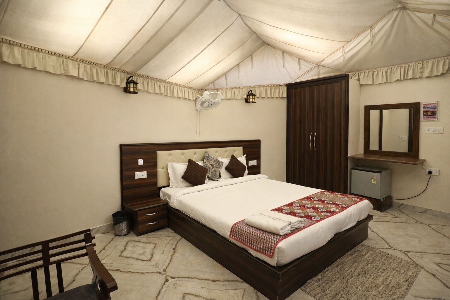 Quarto com cama grande, guarda-roupa, aparador pequeno, espelho e teto com dossel.