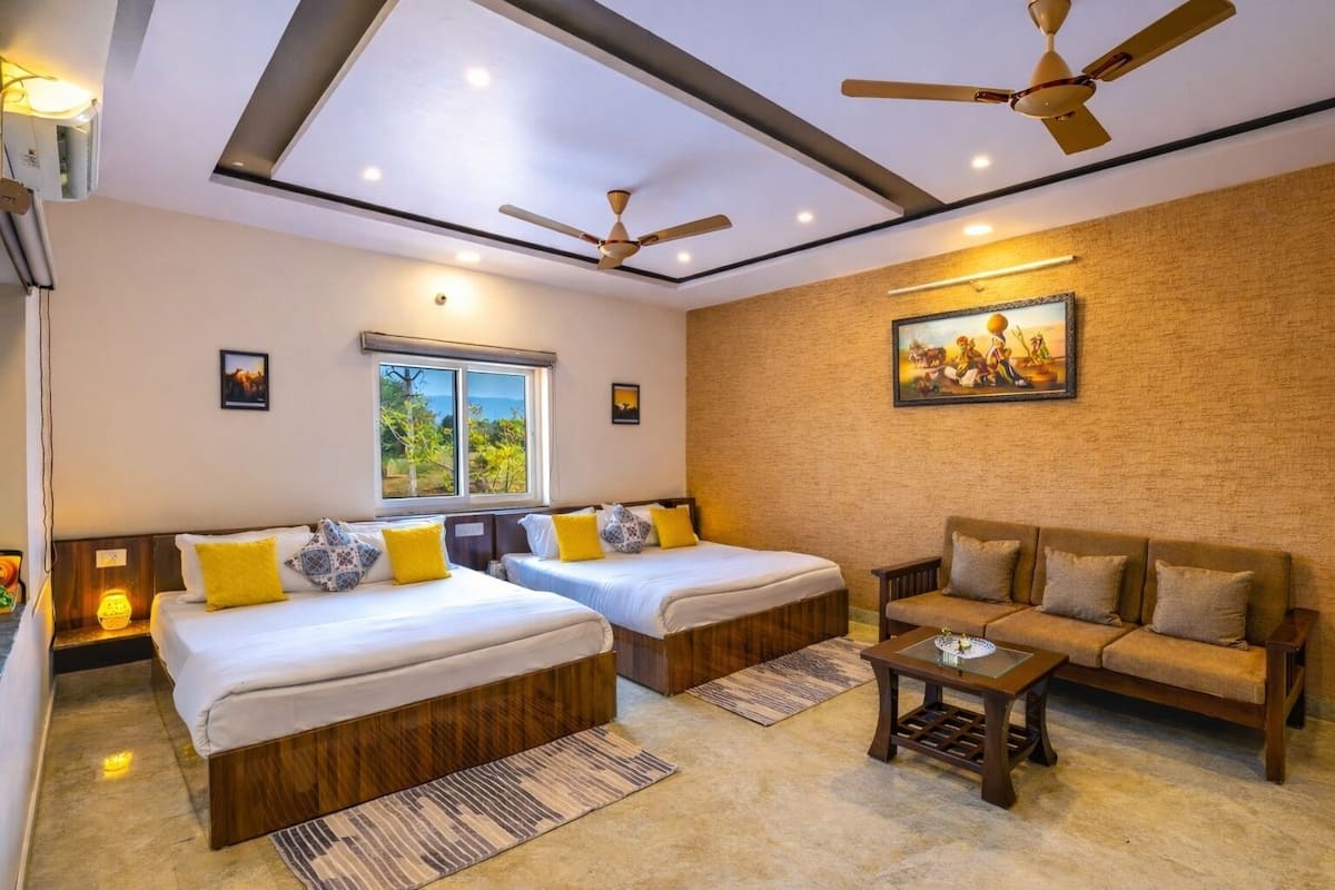 Quarto com duas camas, um sofá, ventilador de teto e janela com vista.