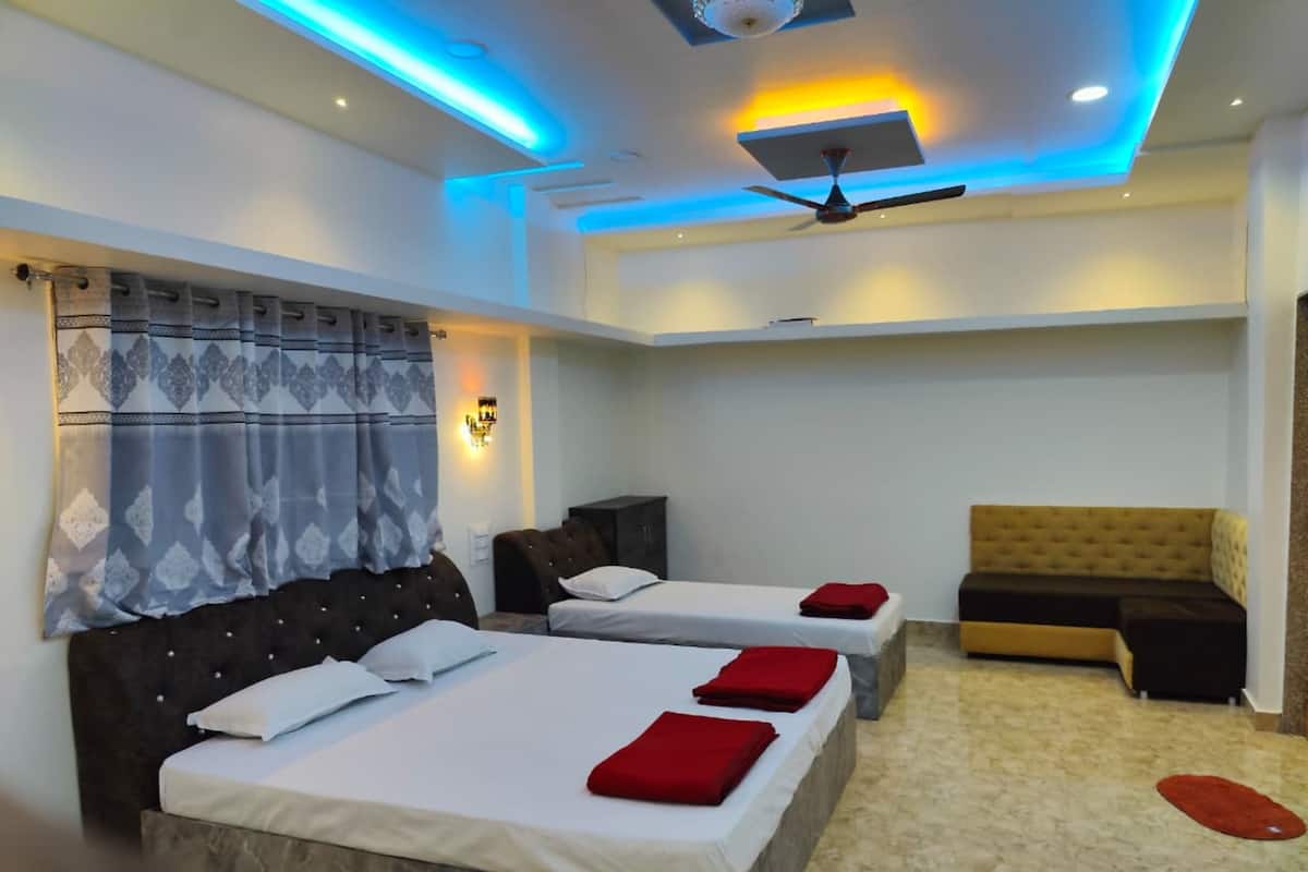 Quarto de hotel com duas camas, um ventilador de teto, um sofá e um tapete vermelho.