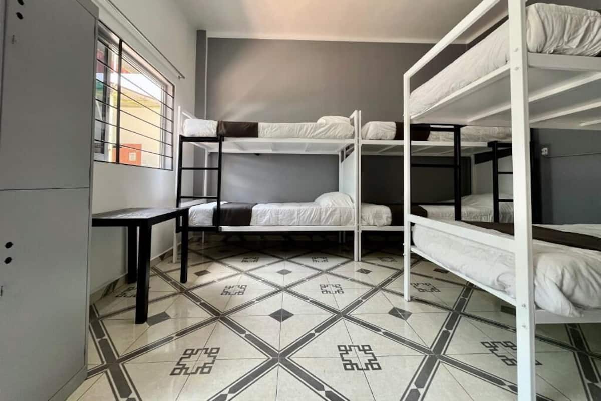 Um quarto tipo dormitório com beliches, uma janela com grades e piso de azulejos.