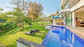 Uma área moderna à beira da piscina, com vista desobstruída, um gramado bem cuidado e um edifício com grandes janelas.