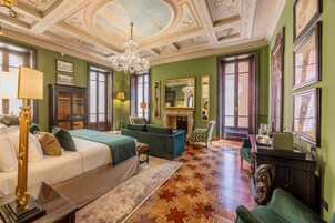 Quarto com cama, sofá, poltrona, lareira e lustre.