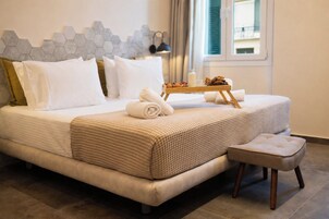 Quarto de hotel com uma cama grande, uma mesa de cabeceira com um prato de petiscos e uma janela com cortinas.