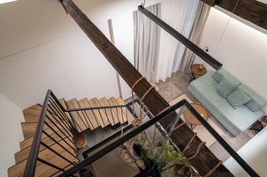 Interior moderno com escada de madeira, sofá azul claro e pequena mesa redonda com um vaso.